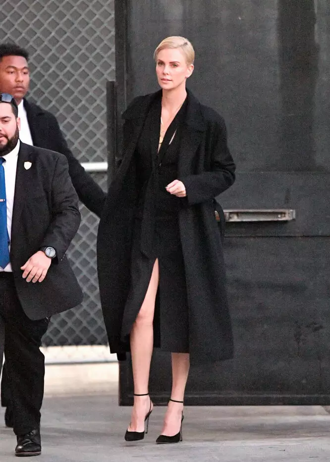 Ο Charlize Theron σε ένα μινιμαλιστικό φόρεμα με μια σαγηνευτική περικοπή σε μια βιασύνη στο γυρίσματα της παράστασης